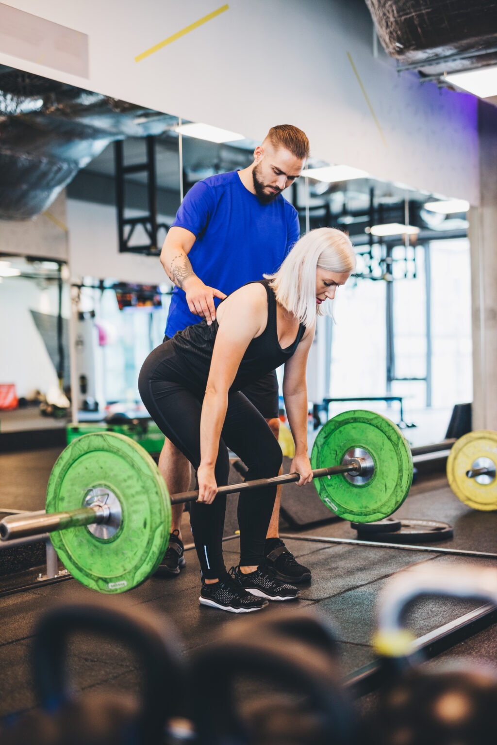Personal trainer assisting woman lifting weights. - Hybrid Fitness